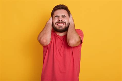 레드 캐주얼 티셔츠를 입고 잘 생긴 수염 남성의 이미지 닫힌 눈과 귀로 포즈를 취하는 매력적인 남자 시끄러운 소음을 듣고 노란색