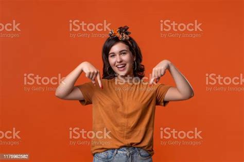 예쁜 갈색 머리 여자 에 티셔츠와 아름 다운 머리띠 가리키는 그녀의 손가락 아래로 오렌지 배경 위에 고립 된 광고를 위한 장소입니다 T 셔츠에 대한 스톡 사진 및 기타