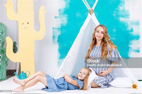 임신 한 어머니와 어린 딸은 청록색 벽의 배경에 가발 근처 재미를 소녀는 어머니의 무릎에 누워 있다 어머니의 날 아기의 날 부활절 2명에 대한 스톡 사진 및 기타 이미지