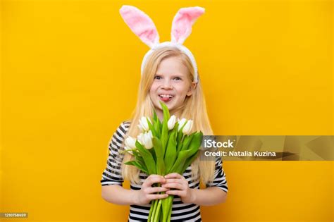 노란색 스튜디오 배경에 머리에 토끼 토끼 귀에 흥분 소녀 쾌활한 미친 미소 행복한 아이는 튤립 꽃다발과 혀를 보여줍니다 부활절과 봄 4월에 대한 스톡 사진 및 기타 이미지