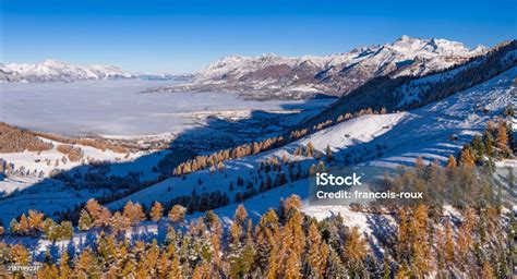 눈 덮인 슬로프와 황금빛 낙엽송이 있는 가을의 Champsaur Valley의 공중 전망 안첼 마을은 아침 안개 속에서 모습을 드러냅니다 오트 알프스 프랑스 0명에 대한