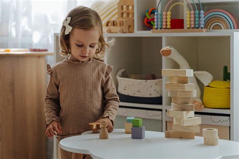 놀이방의 테이블에 나무 블록을 가지고 노는 어린 소녀 현대 보육원에서 아기와 유아를위한 교육 게임 아이는 나무 무지개 쌓기 블록으로 타워를 만듭니다 2 3 살에 대한 스톡