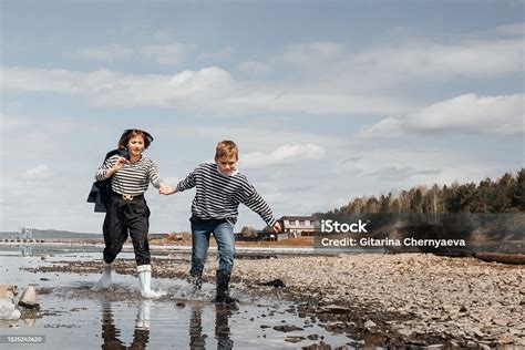 강둑에 있는 엄마와 아들 조끼와 고무 부츠를 입은 엄마와 아들이 물 위에 즐겁게 달려있습니다 10 11세에 대한 스톡 사진 및 기타 이미지 Istock