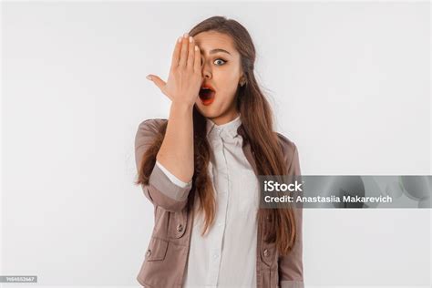 충격을 받은 갈색 머리 소녀의 초상화 얼굴의 절반을 덮고 놀란 얼굴로 카메라를 한 눈으로 바라보고 얼굴의 한쪽에 손바닥을 잡고 흰색 배경 위에 서 있다 20 24세에 대한