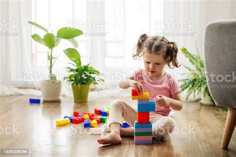 어린 소녀가 놀이방의 바닥에 앉아서 화려한 큐브 생성자를 가지고 놀고 있습니다 놀기에 대한 스톡 사진 및 기타 이미지 놀기