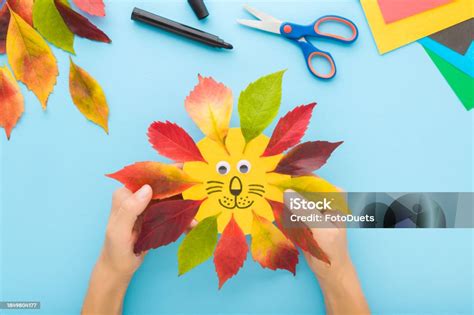 젊은 여자가 손을 들고 파란 테이블 배경에 화려한 나뭇잎과 종이에서 사자 머리 모양을 보여줍니다 파스텔 색상 가을 장식 만들기 시점 샷 근접 촬영 하향식 보기 사자에 대한