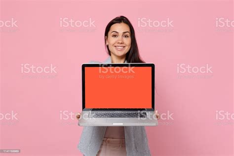 분홍색 파스텔 배경에 고립 된 빈 빈 화면으로 노트북 Pc 컴퓨터를 들고 줄무늬 재킷에 웃는 젊은 여자의 초상화 사람들은 진심으로 감정 라이프 스타일 개념입니다 복사 공간을