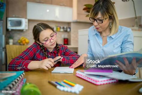 매력적인 젊은 여성과 그녀의 작은 귀여운 딸은 테이블에 앉아 함께 숙제를하고있습니다 어머니는 딸이 학교 수업을 하도록 도와줍니다
