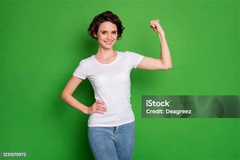 매력적인 자신감 레이디 물결 모양의 머리를 흔들어 완벽한 모양 이두근 팔 승리 경쟁을 착용 캐주얼 흰색 티셔츠 청바지 고립 밝은 녹색 색상 배경의 사진 한 명의 여자만에