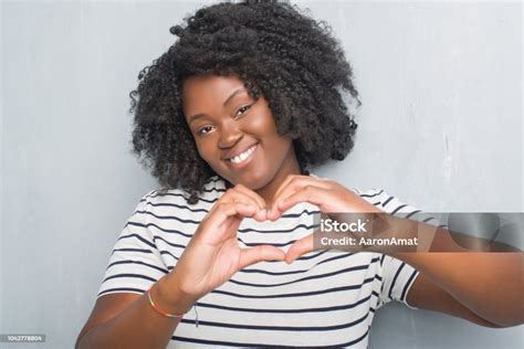 젊은 아프리카계 미국인 플러스 크기 여자 마음 기호와 손으로 모양을 보여주는 사랑에 웃 고 회색 그런 지 벽에 낭만적인 개념입니다 손에 대한 스톡 사진 및 기타 이미지