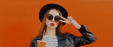 검은 둥근 모자를 쓰고 주스 컵을 가진 세련된 젊은 여성의 초상화 오렌지 색 배경에 재킷 오렌지 감귤류 과일에 대한 스톡 사진