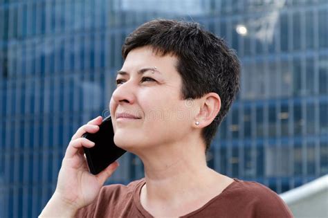 Smiling Woman Talking On Smartphone In Background Of High Rise Building With A Blue Glass Facade