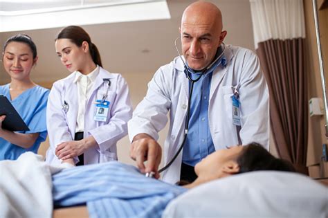 병동을 방문하는 의사 그룹은 여성 환자를 보유하고 침대에서 청진기로 그녀를 확인합니다 의사가 검진을하는 동안 병원 침대에 누워있는 여성 환자 환자에 대한 스톡 사진 및 기타