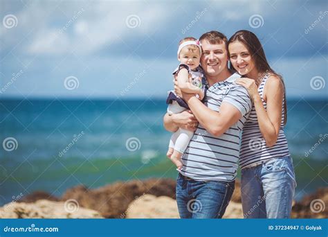 Портрет семьи из трех человек имея потеху совместно берегом океана и наслаждаясь взглядом На