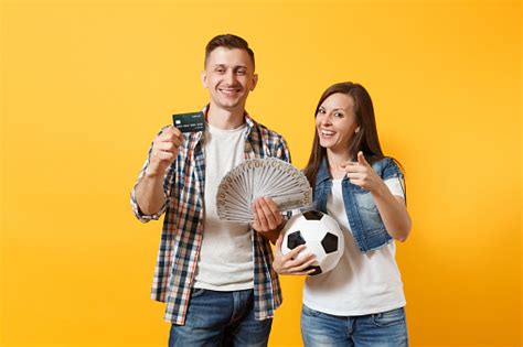 젊은 승 커플 여자 사람 축구 팬 들의 달러 돈 신용 카드 축구공 번들을 들고 노란색 배경에 고립 된 지원 팀을 응원 합니다 스포츠 베팅 열정 가족 라이프 스타일 개념입니다