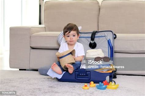 여행에 대 한 준비가 옷의 전체 휴가를 위해 포장 손에 밀 짚 모자를 들고 파란색 가방에 재미 얼굴 표정으로 시 팅과 귀여운 작은 아기 소년 아이와 함께 휴가 가득 찬에