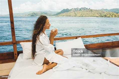 개인 크루즈 투어에서 보트에서 아침 커피를 즐기는 여성 기내 침대 여행과 자유 라이프 스타일 수평선에 코모도 국립 공원의 산 전망 요트 레크리에이션 선박에 대한 스톡 사진