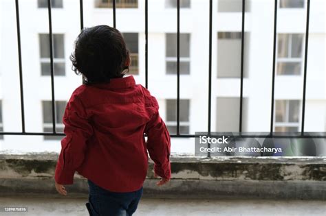 흰색 도시 배경의 발코니에 서있는 동안 활기찬 빨간 셔츠를 입고 인도 귀여운 작은 쾌활한 갈색 머리 타밀 아기 소년의 초상화 2