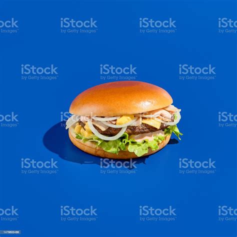 파란색 배경에 양파 체다 치즈 소스를 곁들인 맛있는 치즈버거로 현대적이고 미니멀한 음식 사진 스타일을 반영합니다 이동 중 식사에 적합하며 정사각형 구성으로 제공됩니다 0명에