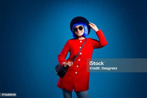 빨간 코트에 쾌활 한 멋진 여자의 바지 편안한 포즈 잡고 가방 선명한 파란색 배경에 고립 된 어깨에 휴식 하는 미소를 전송 하는 데 가발에 대한 스톡 사진 및 기타 이미지