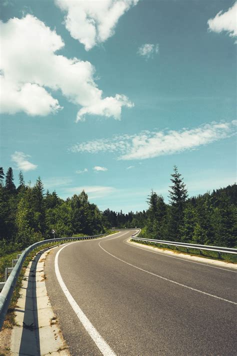 낮에는 푸른 하늘 아래 푸른 나무와 흰 구름 사이의 회색 콘크리트 도로 사진 Unsplash의 무료 길 이미지