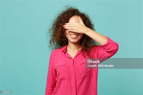 스튜디오에서 파란색 청록색 벽 배경에 고립 된 손으로 눈을 덮고 분홍색 우연한 옷에 웃는 아프리카 소녀의 초상화 사람들은 진심으로 감정 라이프 스타일 개념입니다 복사 공간을