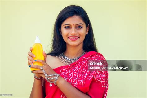 아름답고 웃는 백설 공주 미소 인도 여자 검은 머리카락과 어두운 피부의 초상화 해변에서 자외선 차단제 스프레이 병을 들고 빨간 전통 사리spf 바디 파라다이스 휴가를 즐기는