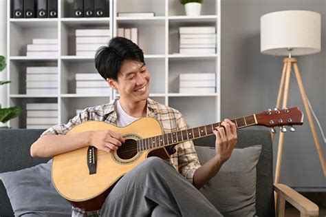 소파에서 어쿠스틱 기타를 연주하는 행복한 남자 아늑한 거실에서 여가 시간을 보낸다 생활 방식에 대한 스톡 사진 및 기타 이미지 생활 방식 음악가 청년 성인 Istock
