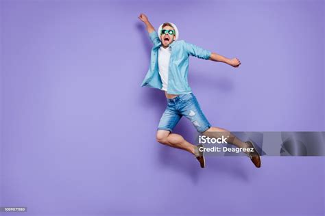 전신 크기 길이 사진 유행 잘생긴 남자의 휴가 입고 캐주얼 청바지 색상 태양 안경 및 Sunhat 구출 하는 공기에서 멀리 서두르고 파스텔 바이올렛 퍼플 배경 위에 속이 고