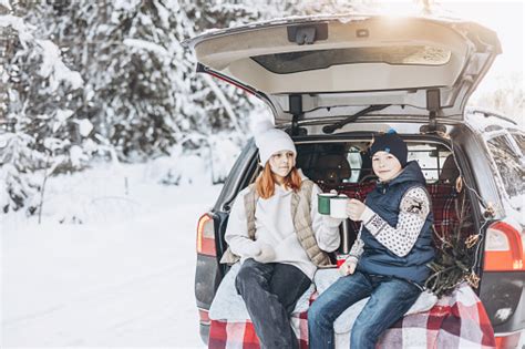 크리스마스를 위해 장식 된 자동차 트렁크에 보온병이있는 두 친구 십대 소년과 소녀 도로 여행 모험과 지역 여행 개념 눈 덮인 숲에서 겨울 피크닉 새해 휴가 12 13세에
