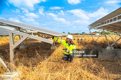 안전 장비를 착용한 기술자가 맑고 푸른 하늘과 흩어져 있는 흰 구름을 배경으로 풀이 무성한 태양광 발전소에서 전동 드릴을