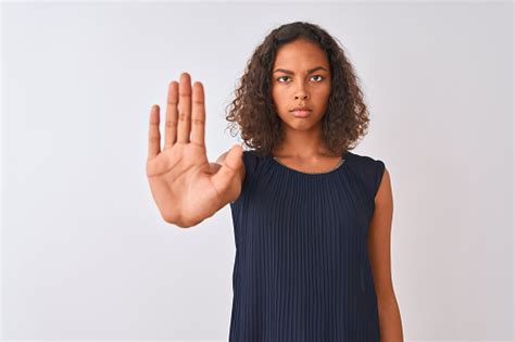 고립된 흰색 배경 위에 파란색 드레스를 입은 젊은 브라질 여성이 손바닥으로 노래를 멈추고 있습니다 얼굴에 부정적이고 심각한