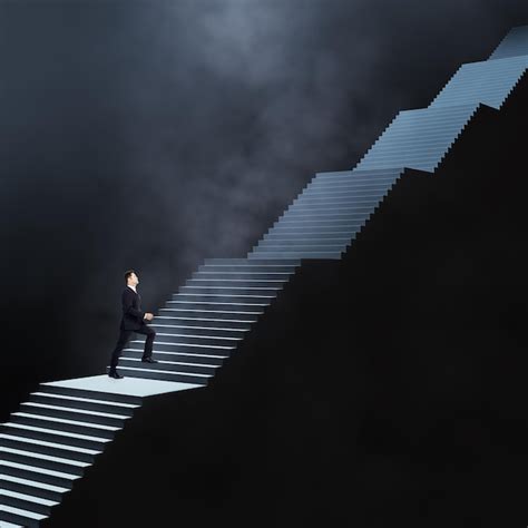 사업가와 함께 긴 경력과 성공 개념에 이르는 긴 길은 추상적인 어두운 안개 배경에서 위에서 조명되는 어두운 계단을 올라갑니다 프리미엄 사진