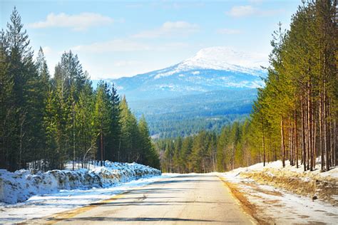 복엽수 림을 통과하는 빈 아스팔트 도로의 전경 배경에 눈 덮인 산 겨울 풍경입니다 콜라 반도 무르만스크 지역 폴라 서클 카렐리아 러시아 겨울에 대한 스톡 사진 및 기타