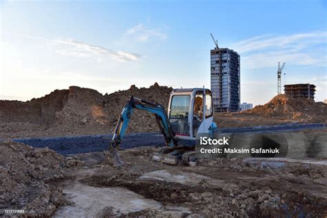 일몰 배경에 건설 현장에서 토공 하는 동안 미니 굴삭기 무단 전침 기계 도로 공사의 백호는 콘크리트 연석과 포장 슬래브를