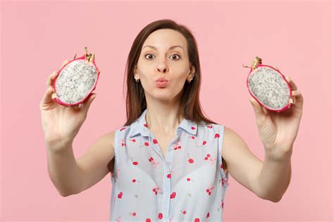 예쁜 어린 소녀는 분홍색 파스텔 벽 배경에 고립 된 신선한 익은 피타 야 용 과일의 Halfs를 들고에 어 키스를 보내는 불어