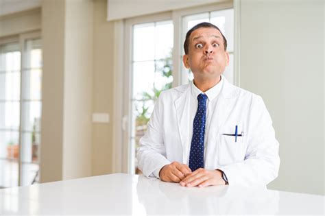 중 기 닥터 남자는 재미 있는 얼굴로 퍼 핑 뺨 클리닉에서 의료 코트를 입고 입에 공기 미친 표정으로 팽창 공기 주입에 대한 스톡 사진 및 기타 이미지 Istock