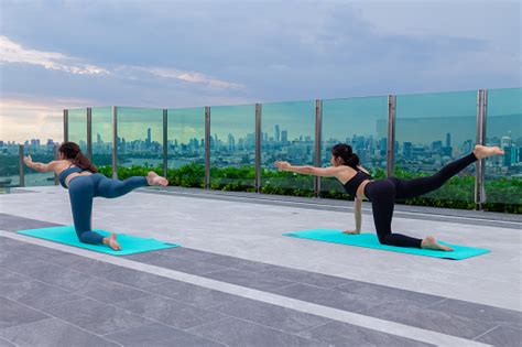 젊은 아시아 여성 플렉시블 슬림은 운동을 분할하고 요가나 필라테스를 연습합니다 큰 건물의 지붕에 여자 자연의 아름다움과 웰빙