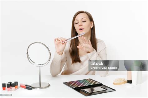 매력적인 여자 수정 손톱을 사용 하 여 실패 흰색 바탕에 격리 설정된 얼굴 장식 화장품으로 메이크업을 적용 하는 테이블에 앉아 손톱 뷰티 여성 패션 라이프 스타일 개념입니다