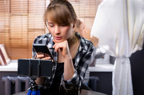 여성 블로거 인플루언서가 사무실 테이블에 앉아 전화를 들고 있습니다 소녀 동영상 블로거 촬영 소셜 미디어 게시물 스마트폰많은 좋아하는 이모티콘을 얻을 클로즈업 보기입니다