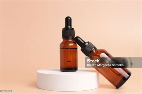 베이지 색 배경에 제품 프리젠 테이션을위한 흰색 연단에 호박 색 유리 드롭퍼 병 다른 크기 스킨케어 제품 천연 화장품 얼굴을 위한 뷰티 컨셉 베이지 배경에 대한 스톡 사진