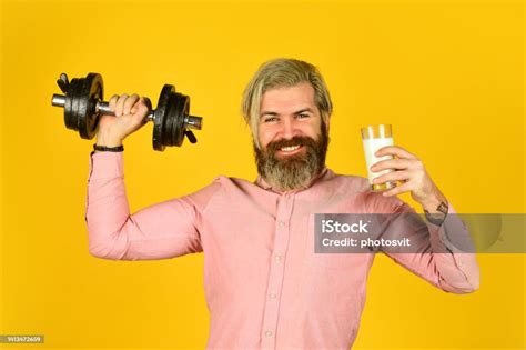 칼슘의 공급원 수염을 가진 남자는 우유를 마신다 체육관에서 운동하십시오 우유 좋은 영양소 지방의 양 근육을위한 비타민 스포츠맨은 덤벨과 우유 한 잔을 들고 있습니다 단백질