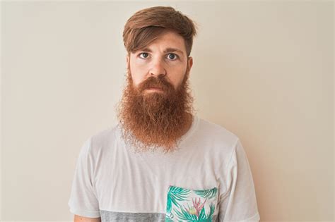 젊은 빨간 머리 아이리쉬 남자 입고 T 셔츠를 입고 고립 된 흰색 배경 위에 서 있고 스마트 한 얼굴에 자신감 있는 표정으로 심각한 생각 T 셔츠에 대한 스톡 사진 및 기타