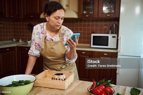 신선한 야채를 절임하는 조리법을 살펴보고 부엌 섬에 서있는 재료를 비교하는 아름다운 여성 Brand Name Smart