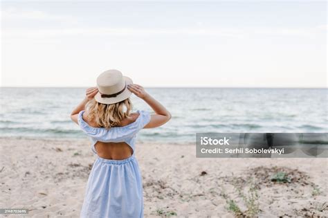 모래에 세련 된 여성의 초상화입니다 해변 바다에 서서 휴가에 화창한 여름 행복한 날을 즐기는 아름 다운 소녀 뒷모습 밀짚모자를 쓴 젊고 매력적인 금발 여자가 즐겁게 바다
