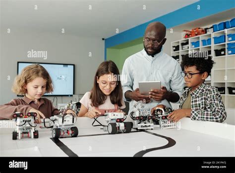 Young Confident African American Teacher Of Robotics With Tablet Helping Cute Intercultural