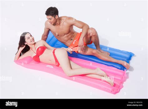Woman In Red Bikini Lying On Her Side On A Float With Her Head Rested On Her Hand And A Man In