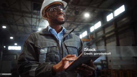 안전 유니폼과 하드 햇을 착용한 전문 중공업 엔지니어 작업자는 태블릿 컴퓨터를 사용합니다 금속 건설 제조에서 걷는 아프리카 계