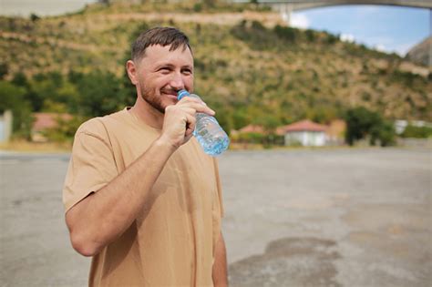 수염을 기른 자신감 넘치는 젊은 잘생긴 남자가 플라스틱 병에서 물을 마시고 더운 여름날 산의 경치를 즐기고 있다 의료 개념입니다