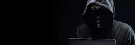 Premium Ai Image Hacker Without Face In A Hood Holds A Laptop On A Dark Background Banner